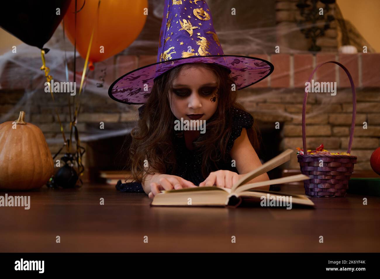 Little girl looking like a witch in wizard hat, lying on the floor ...