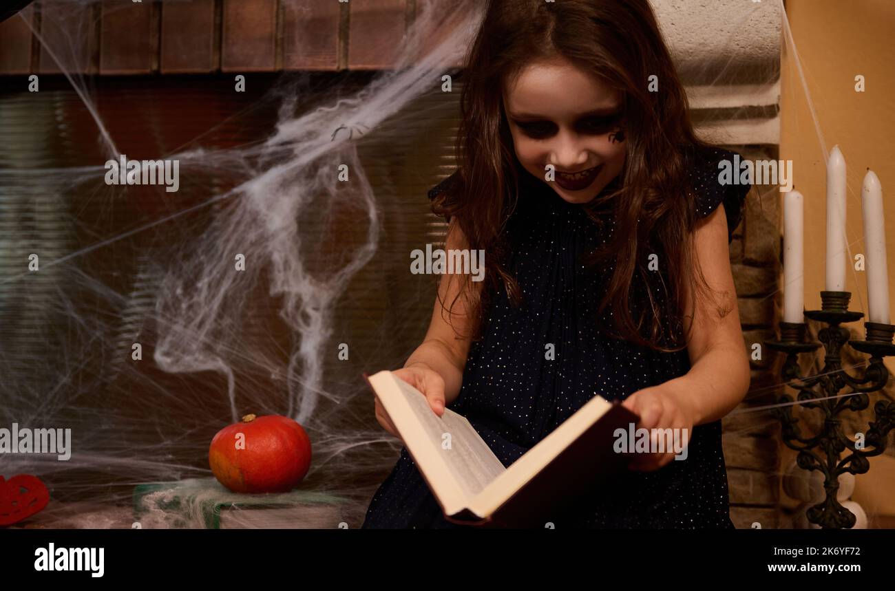 Gothic baby girl with a book of sorcery, sitting by a fireplace with ...