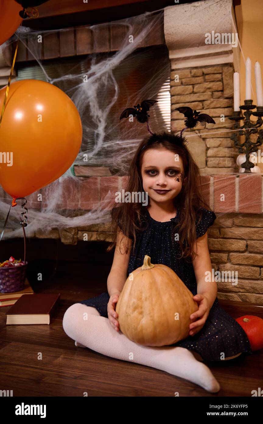 Little girl with smokey eyes, in black dress and hoop with bats, holds ...