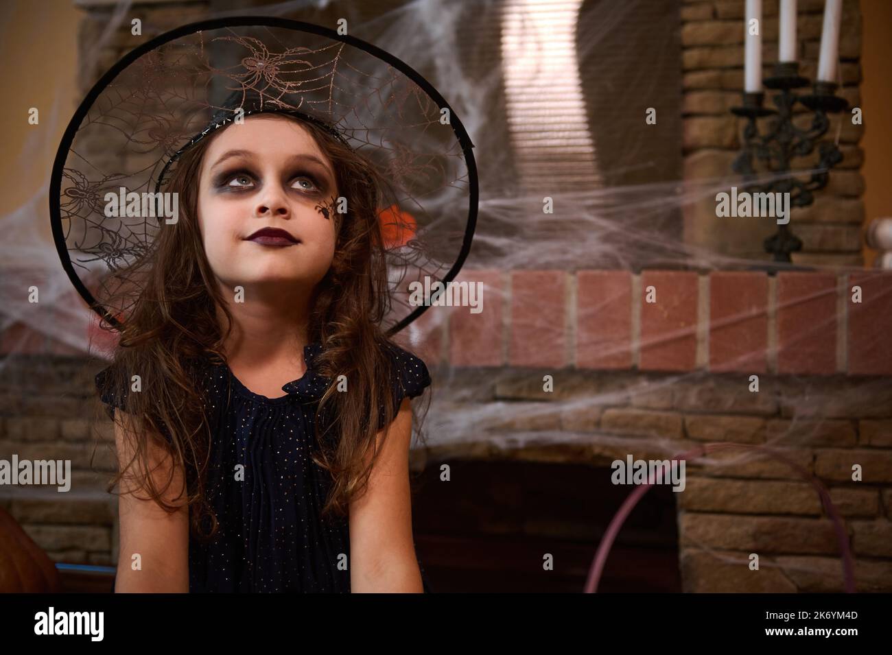 Mysterious little girl in black dress and wizard's hat sits against a ...