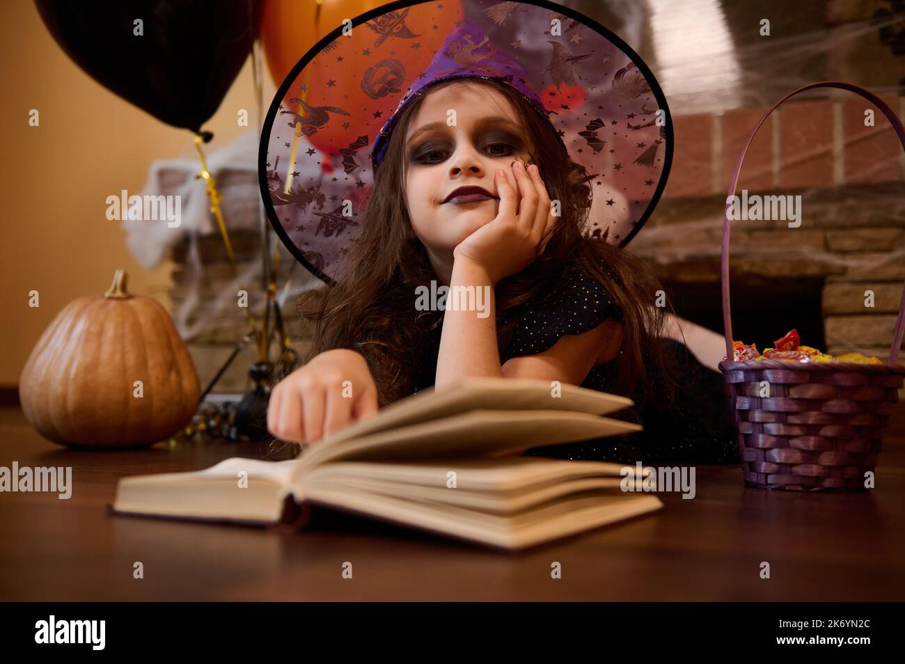 Little girl with face art make-up, in wizard hat, lying on the floor ...