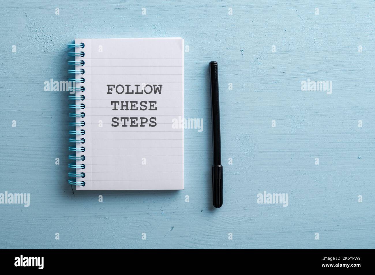 Spiral notebook with a Follow these steps sign placed over pastel blue ...