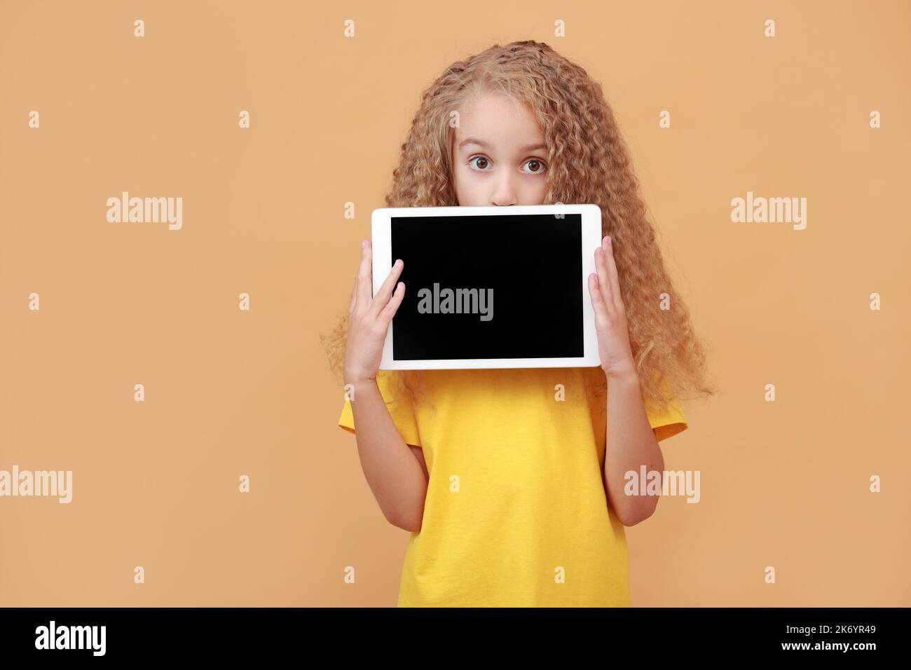 Amazed kid in hiding behind digital tablet with empty screen over ...