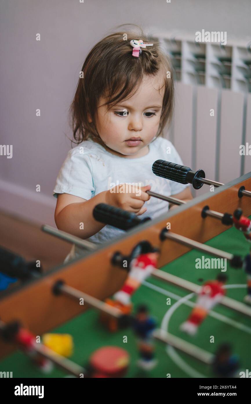 The curious baby girl standing by the football table watching her ...