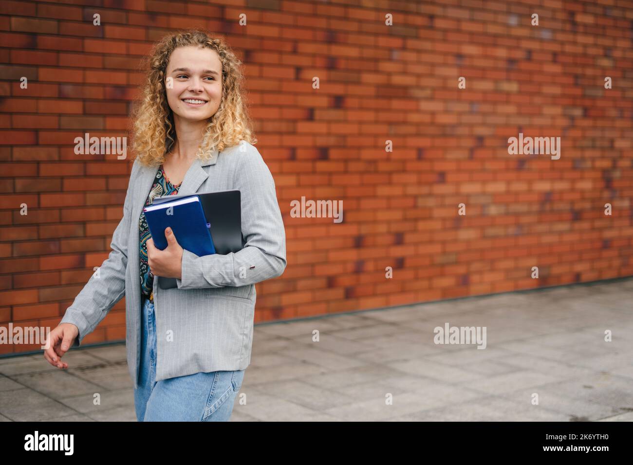 Portrait of smiling woman student holding laptop computer looking away ...