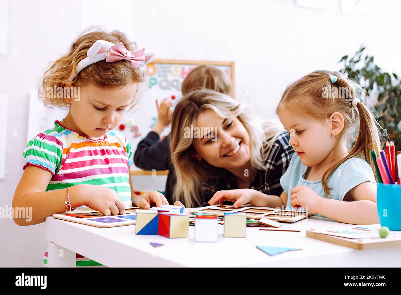 Female teacher with children have fun in development center. Writing ...