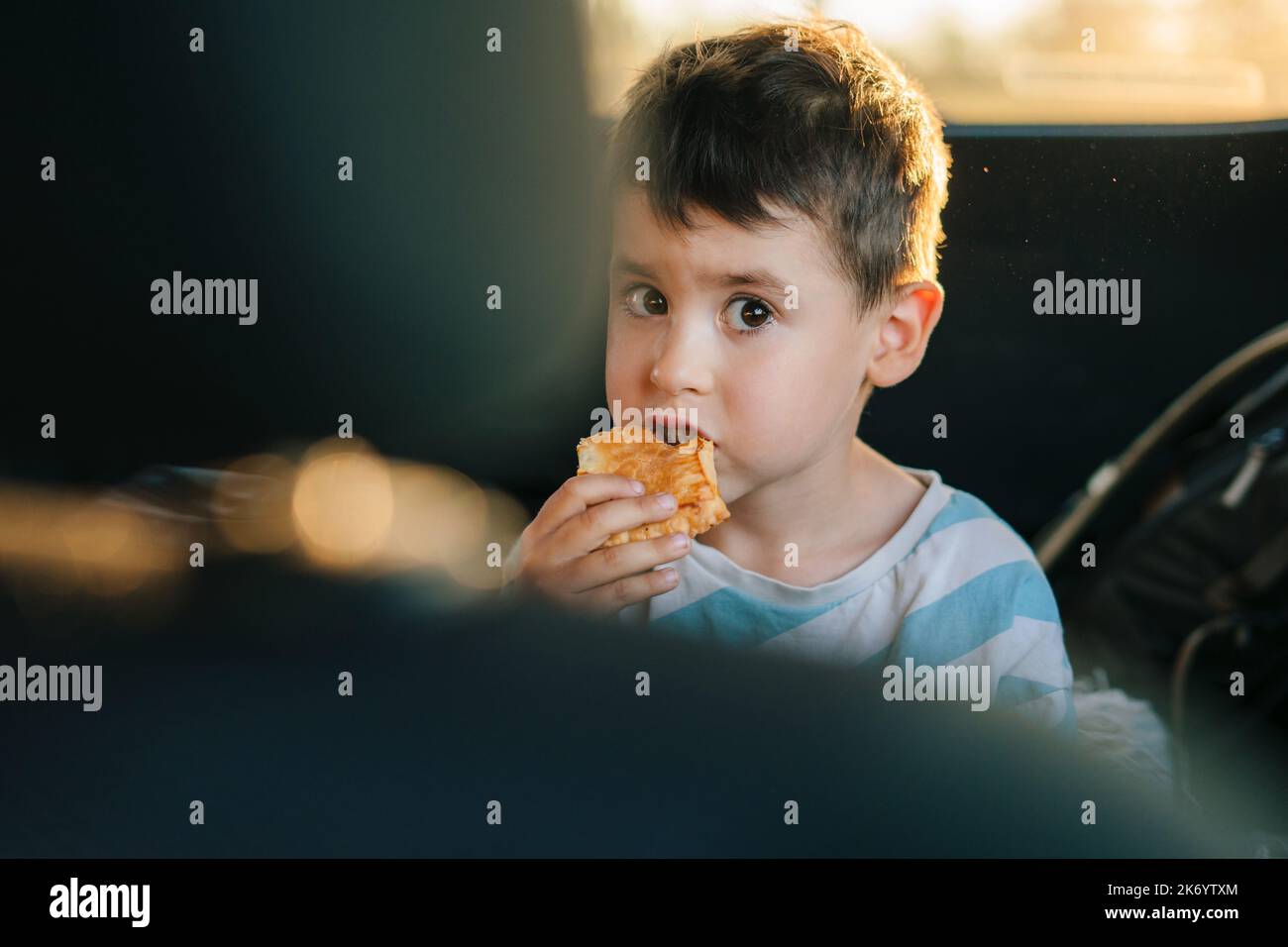 Happy child eating a pie in the car, holding a snack to eat in his ...