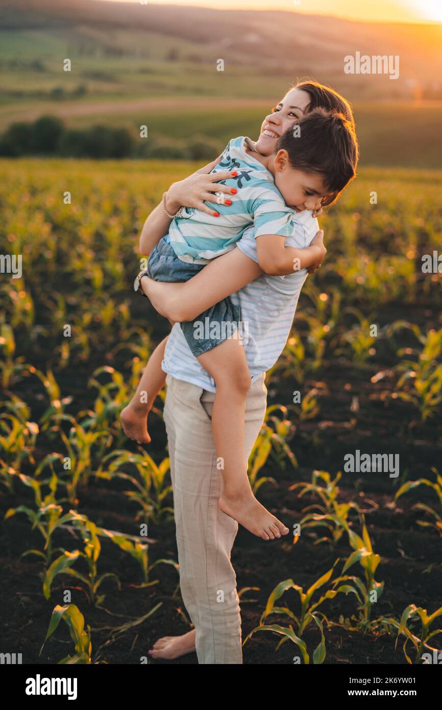 Side view of a preschooler boy being held by her mothering a corn field ...