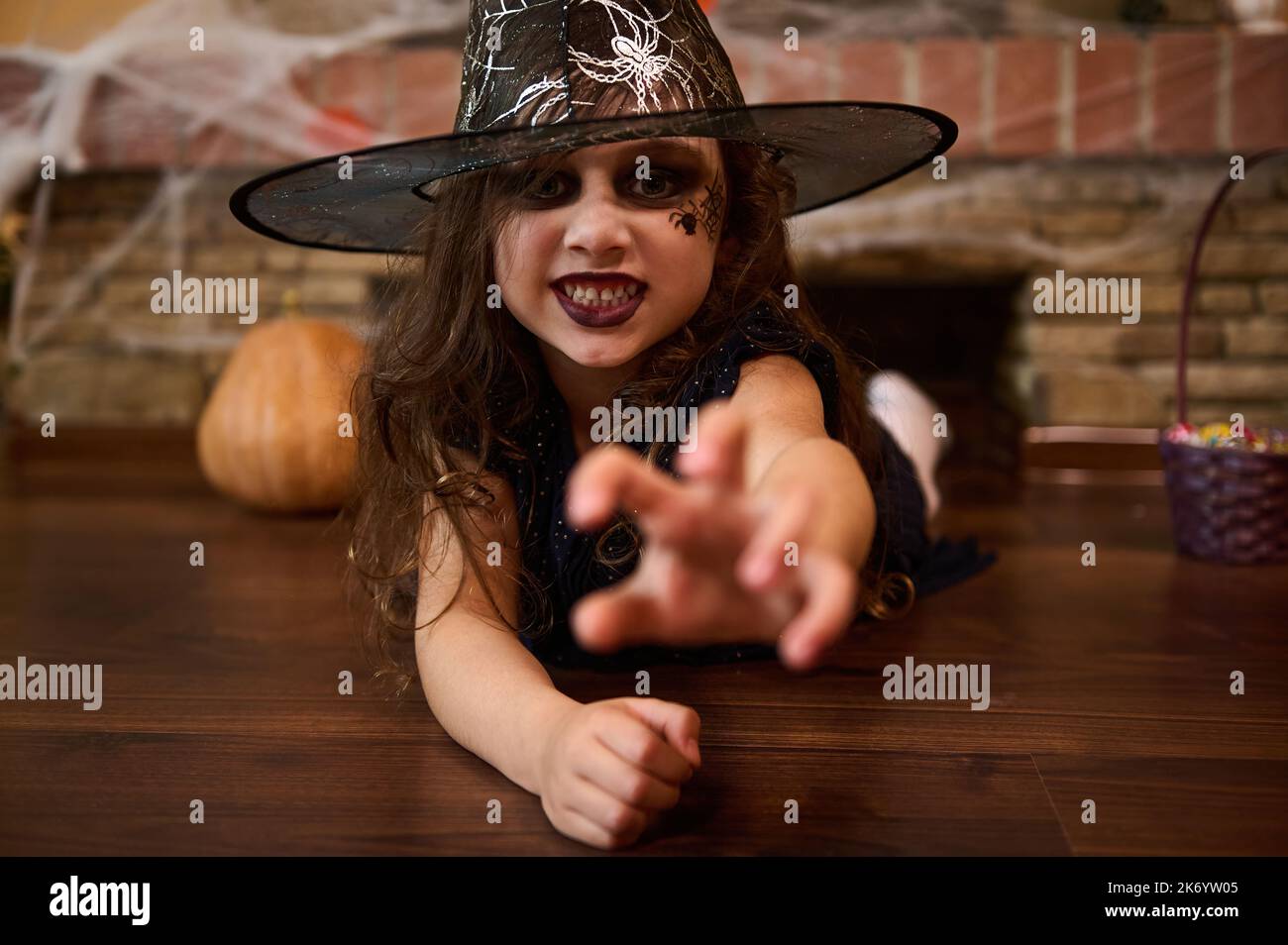 Little girl witch in a wizard's hat, stretches out her hand, looks at ...