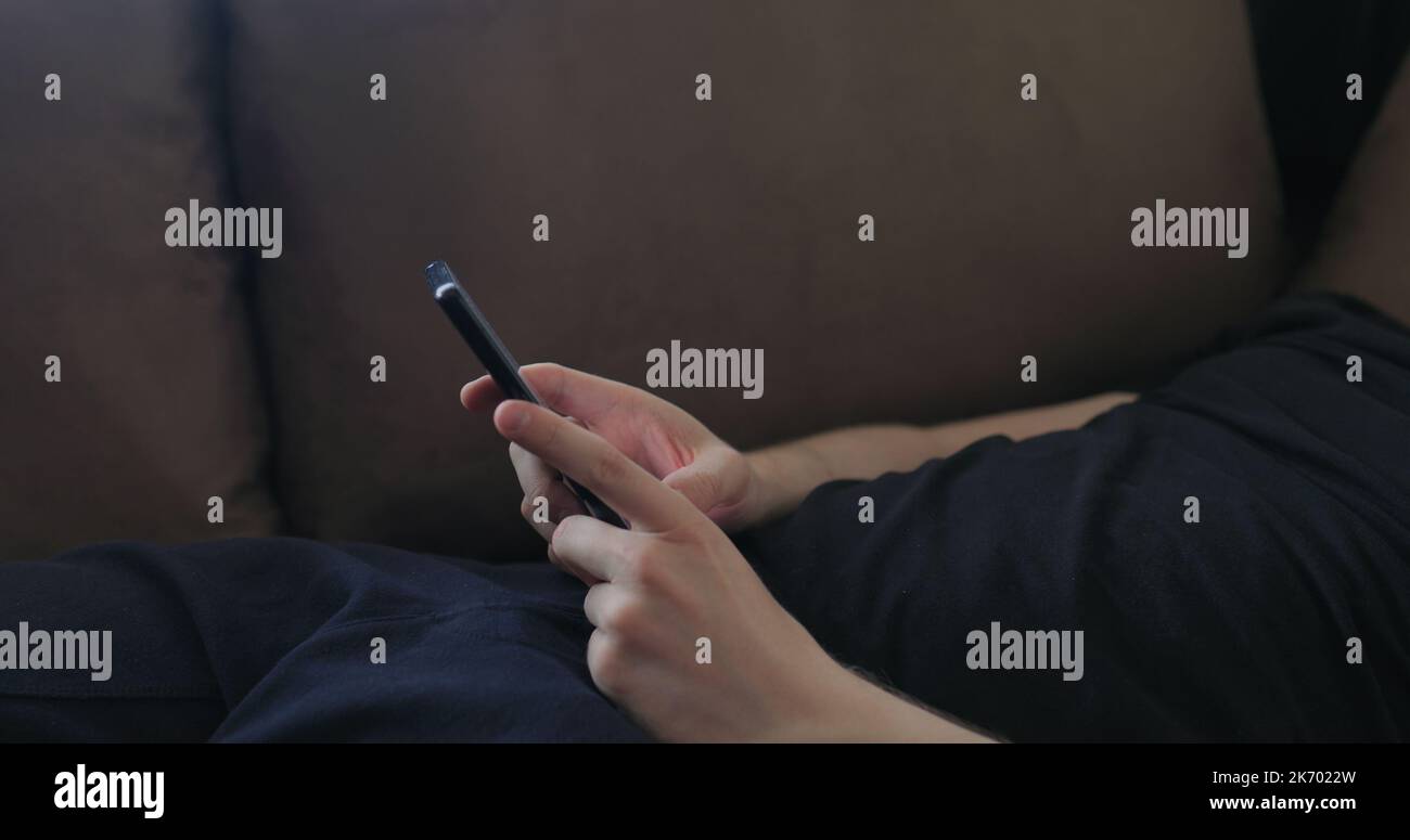 Closeup young man use smartphone working from home lying on couch side ...