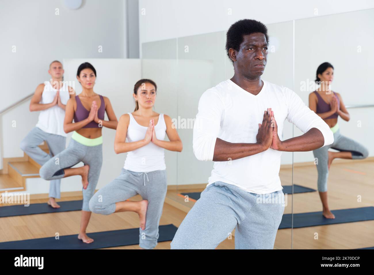 Focused aframerican standing in Eka Pada Pranamasana during group yoga ...