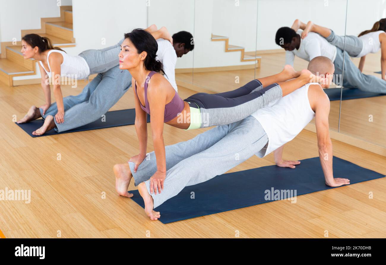 Women and men performing paired yoga exercises during group training ...