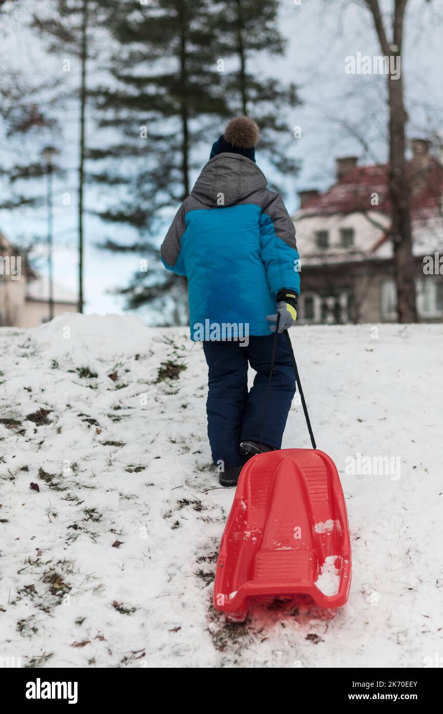 A child with a red sled climbing a snow slide Stock Photo - Alamy