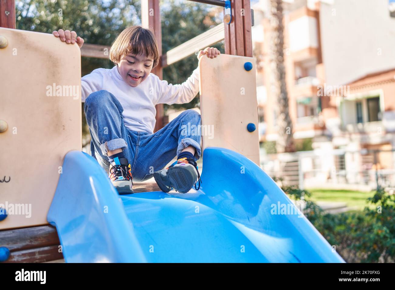 Down syndrome kid smiling confident playing on slide at park Stock Photo - Alamy