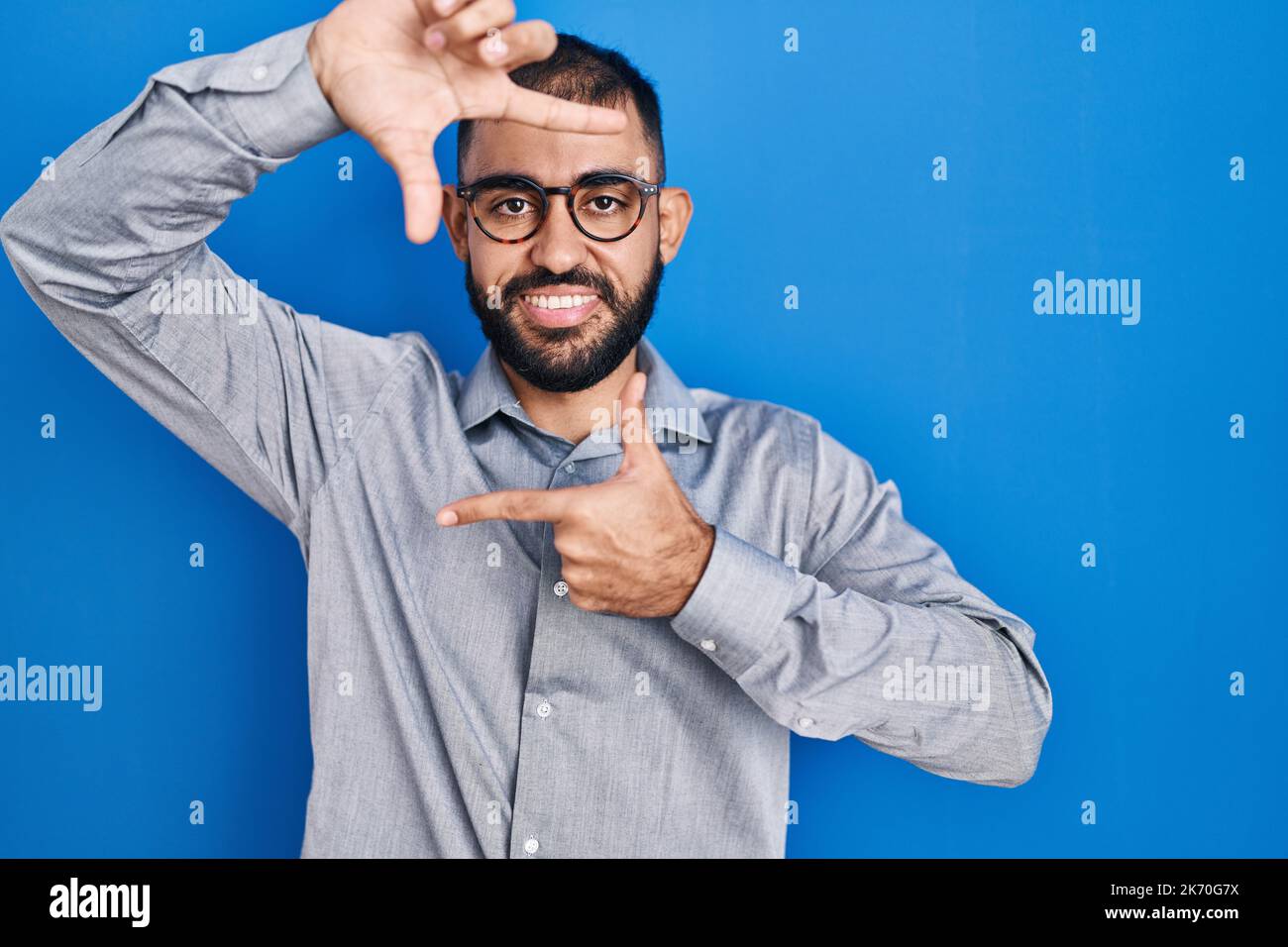 Middle east man with beard standing over blue background smiling making ...