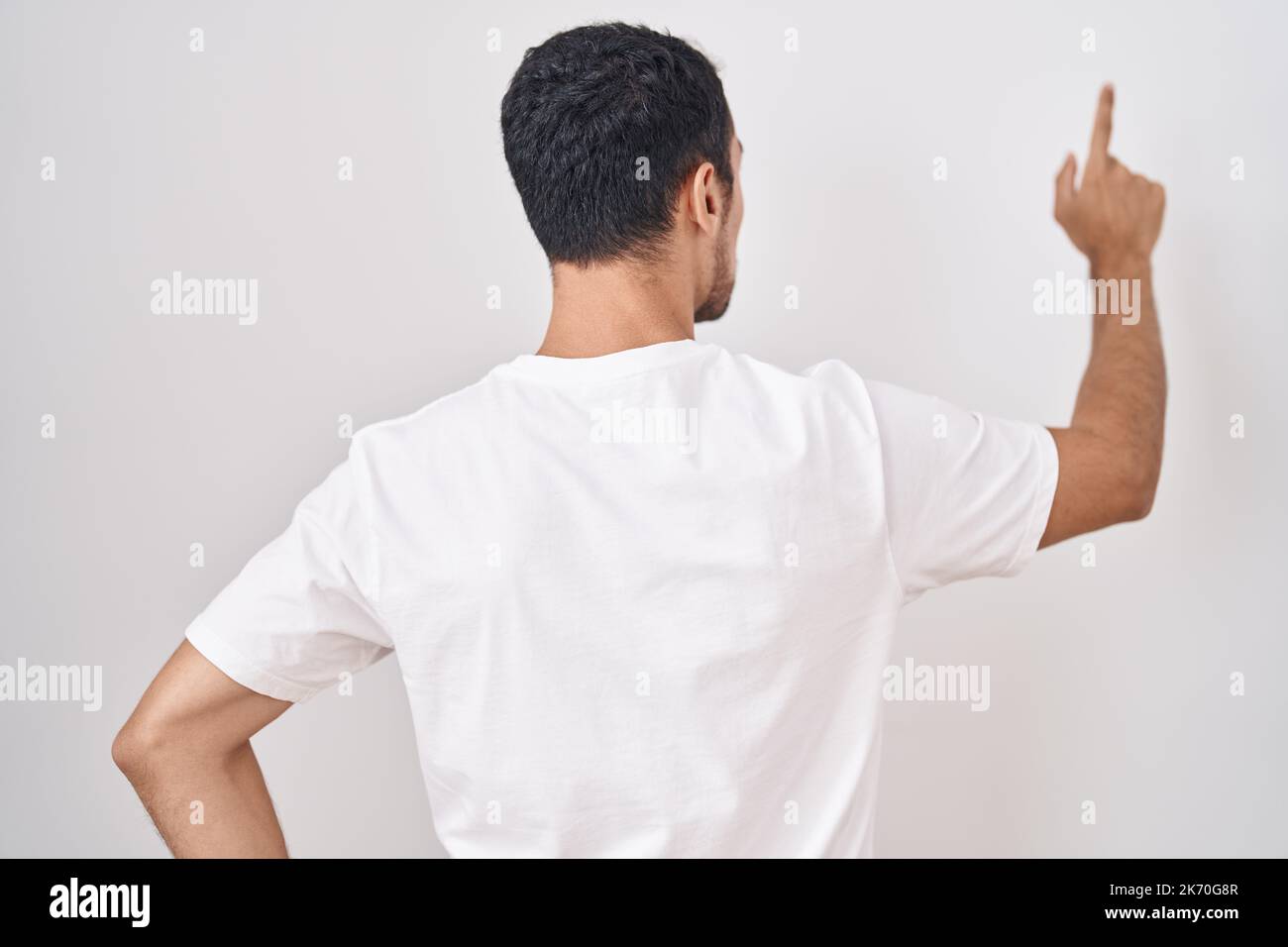Handsome hispanic man standing over white background posing backwards ...