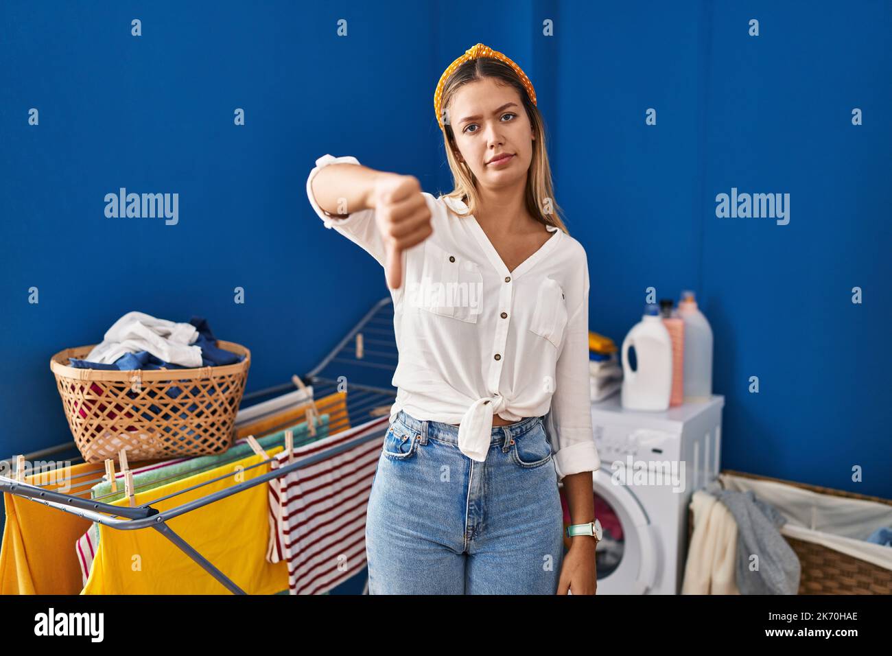 Young blonde woman at laundry room looking unhappy and angry showing ...