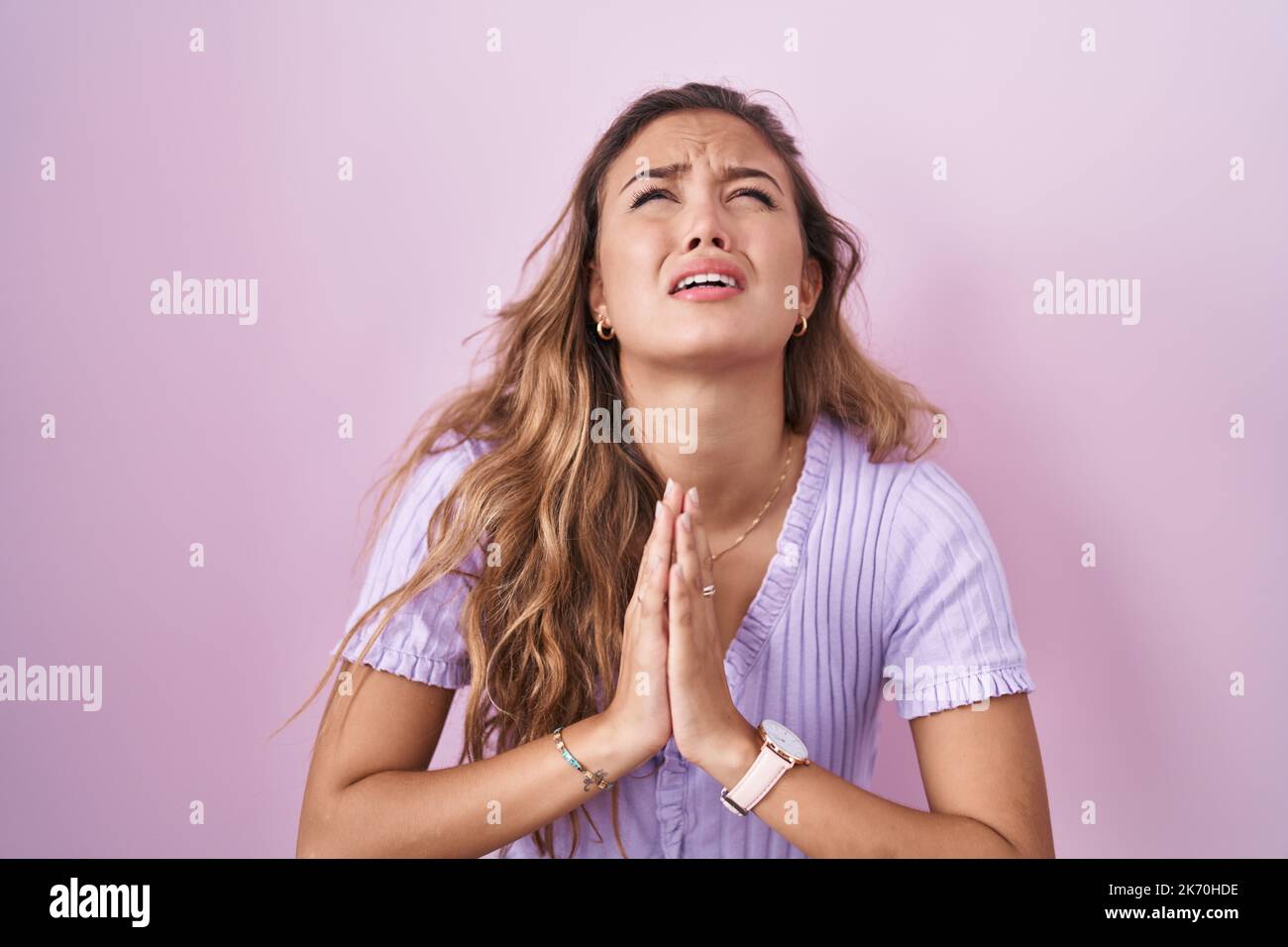 Young hispanic woman standing over pink background begging and praying ...