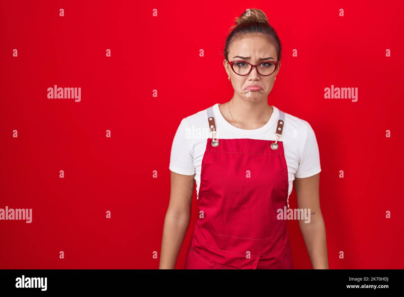 Young hispanic woman wearing waitress apron over red background ...
