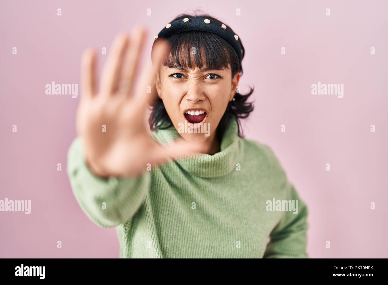 Young beautiful woman standing over pink background doing stop gesture ...
