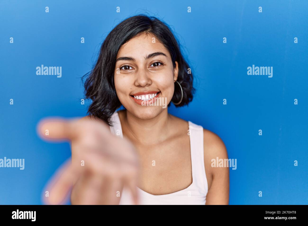 Young hispanic woman standing over blue background smiling friendly ...