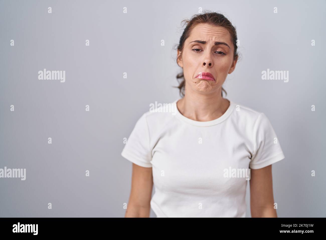 Beautiful brunette woman standing over isolated background depressed ...