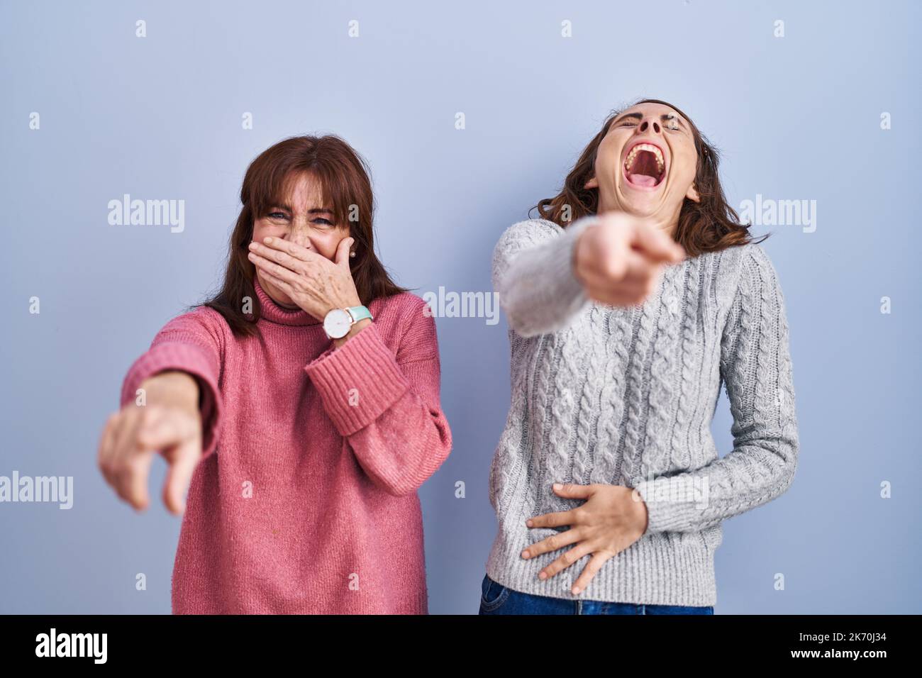 Mother and daughter standing over blue background laughing at you ...
