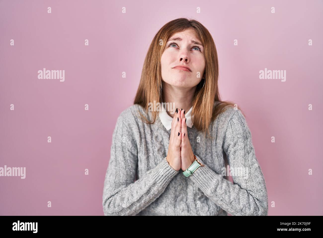 Beautiful woman standing over pink background begging and praying with ...