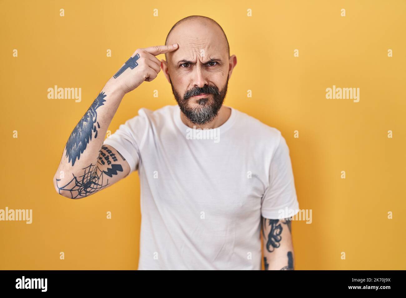 Young hispanic man with tattoos standing over yellow background ...