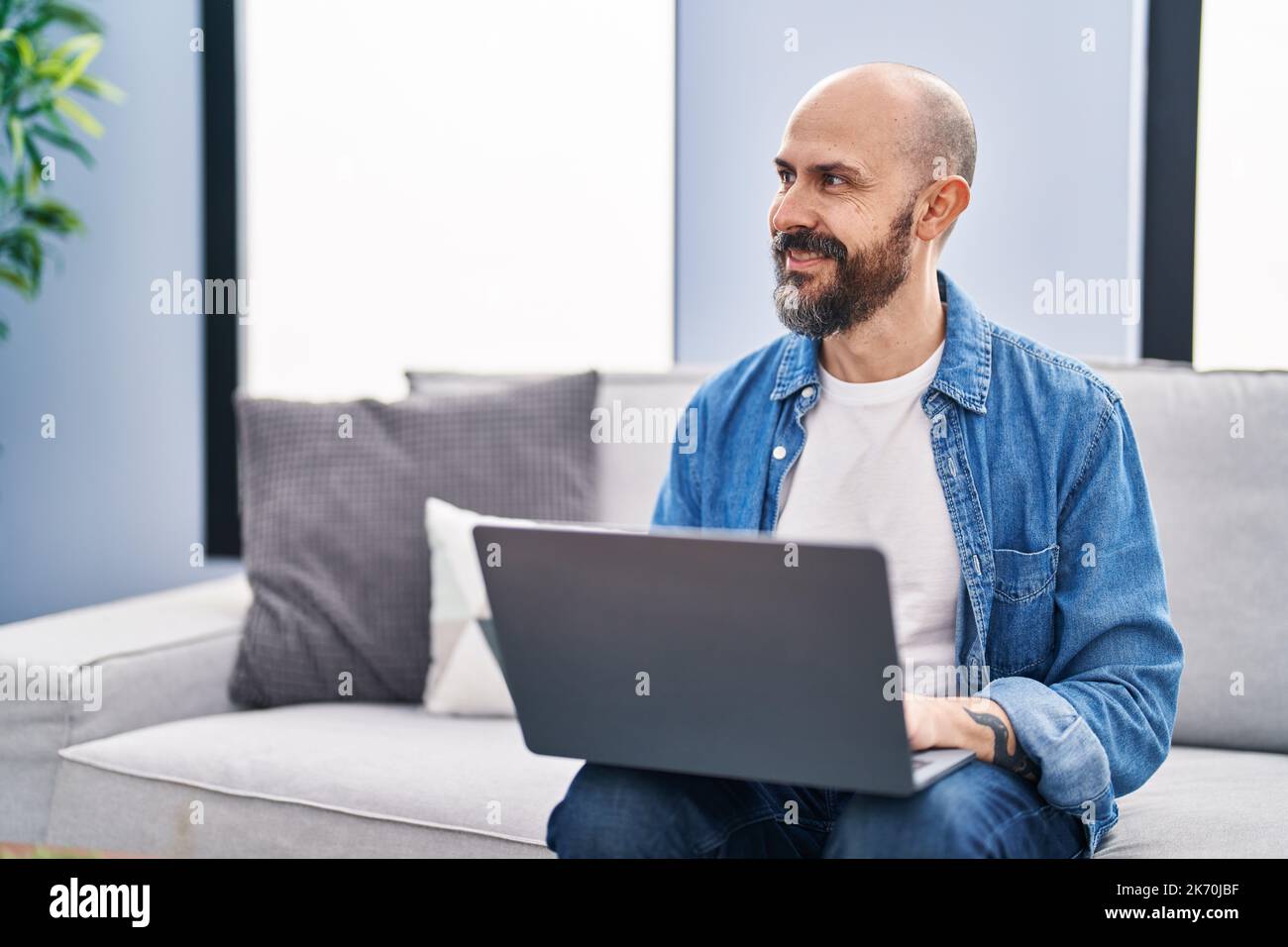 Young bald man using laptop sitting on sofa at home Stock Photo - Alamy