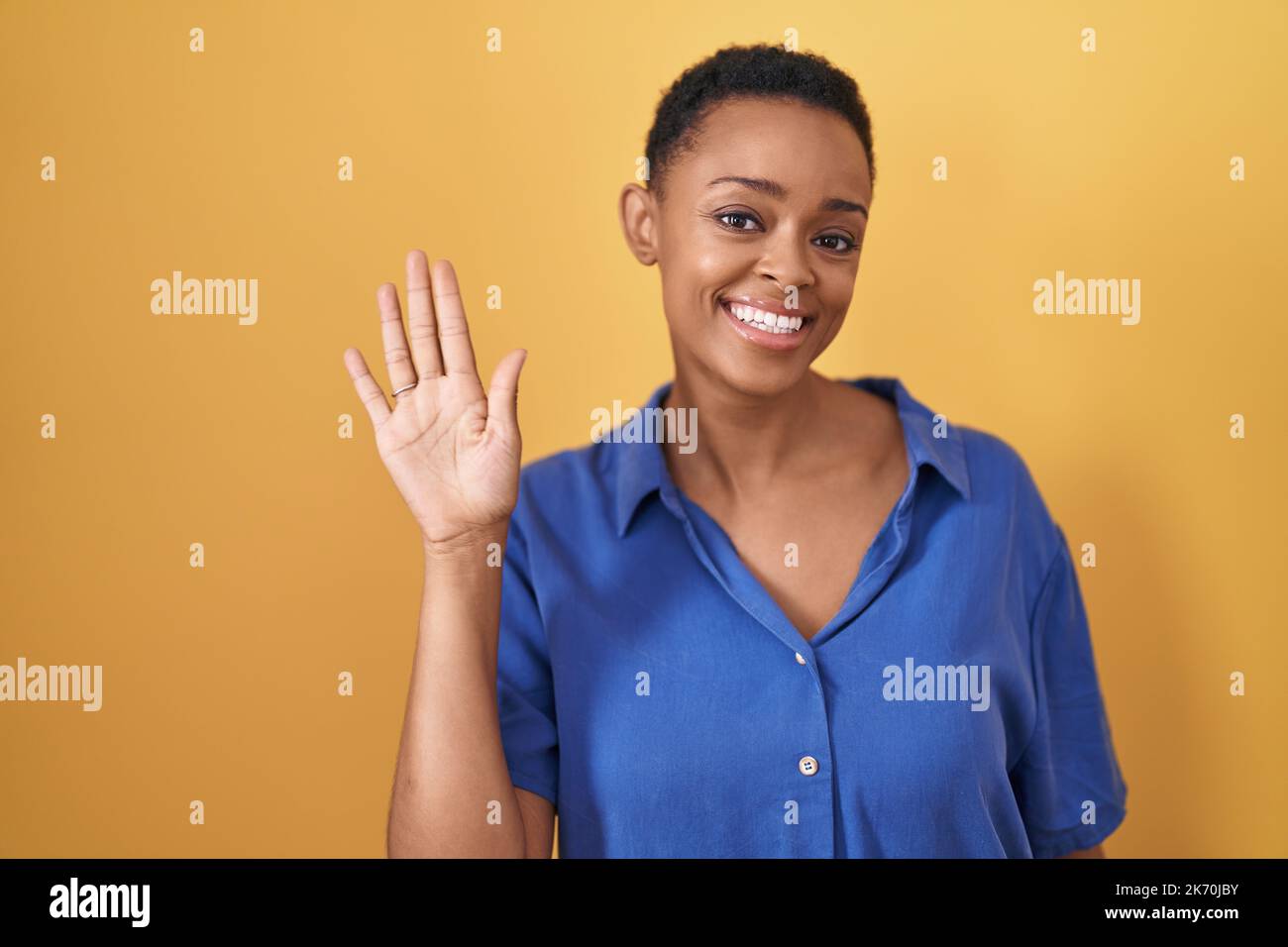 African american woman standing over yellow background waiving saying ...