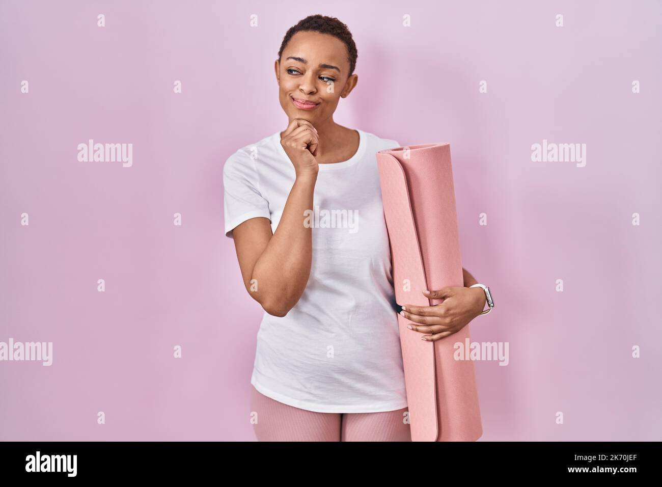 Beautiful african american woman holding yoga mat with hand on chin ...