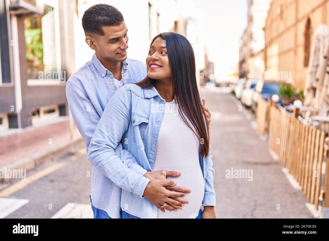 Young latin couple expecting baby hugging each other standing at street Stock Photo - Alamy