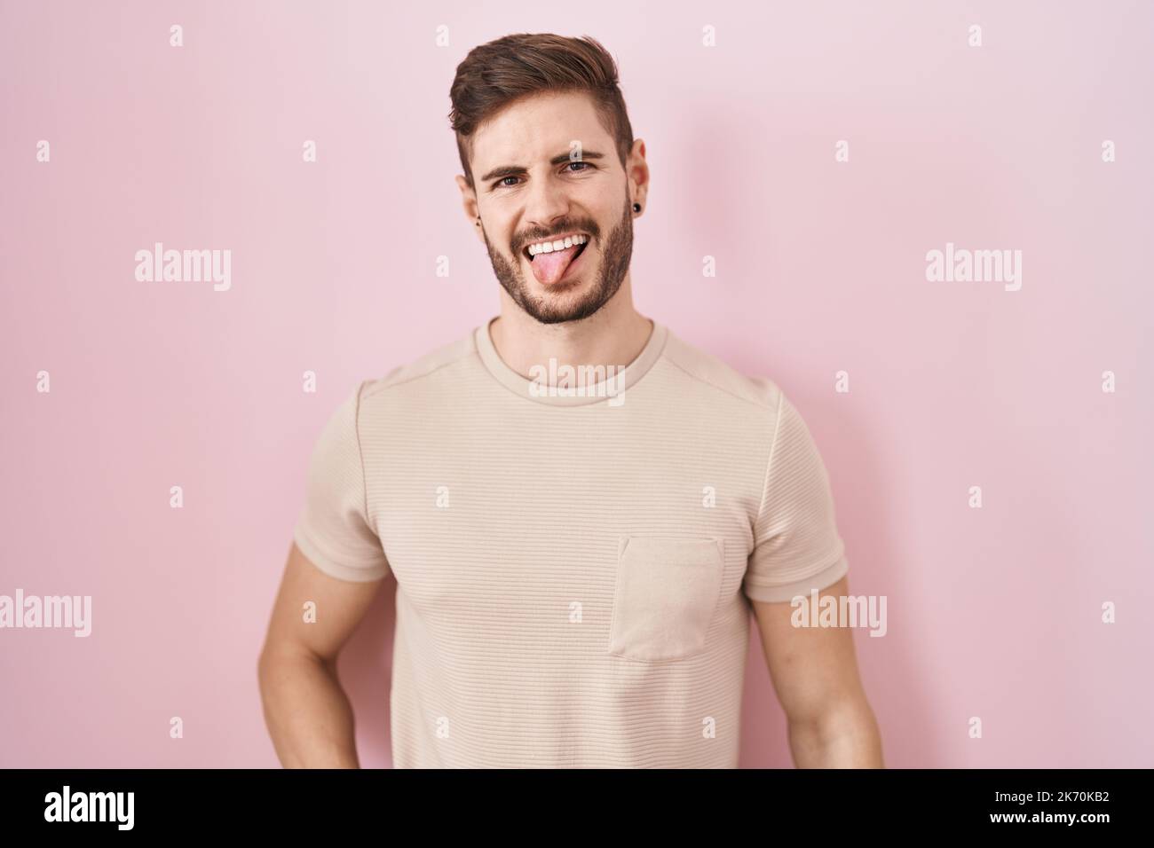 Hispanic man with beard standing over pink background sticking tongue ...