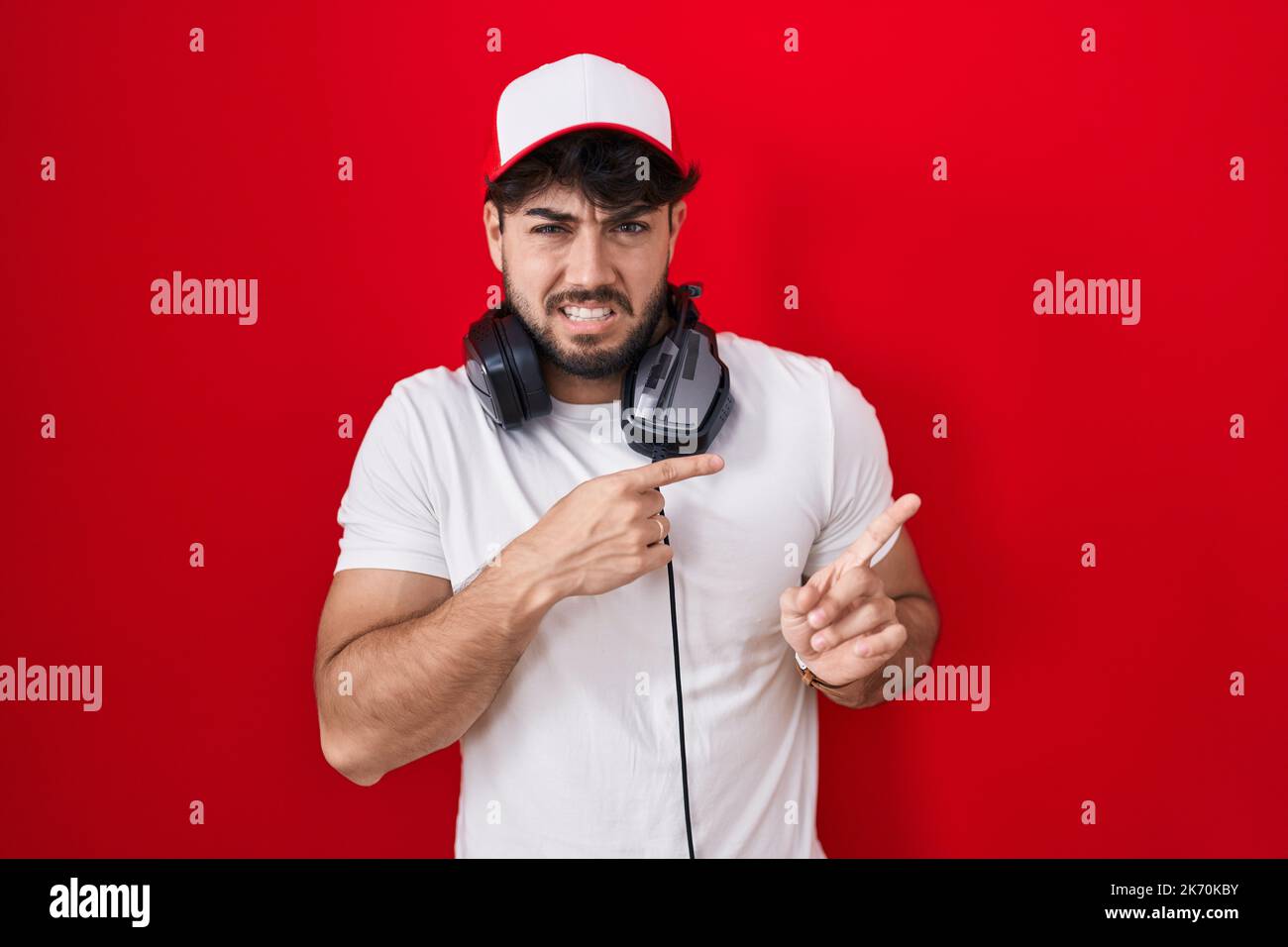 Hispanic man with beard wearing gamer hat and headphones pointing aside ...