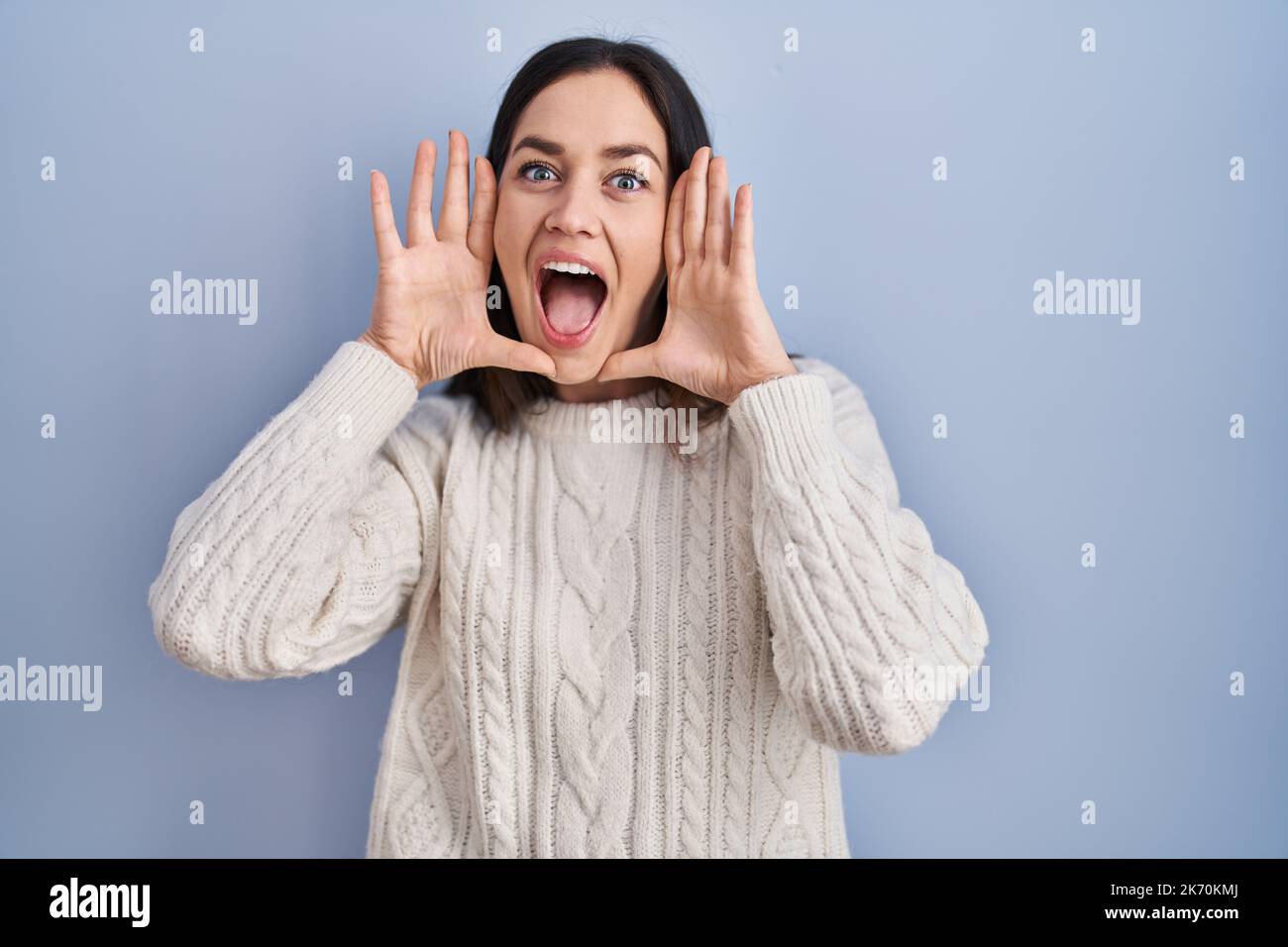 Young brunette woman standing over blue background smiling cheerful ...