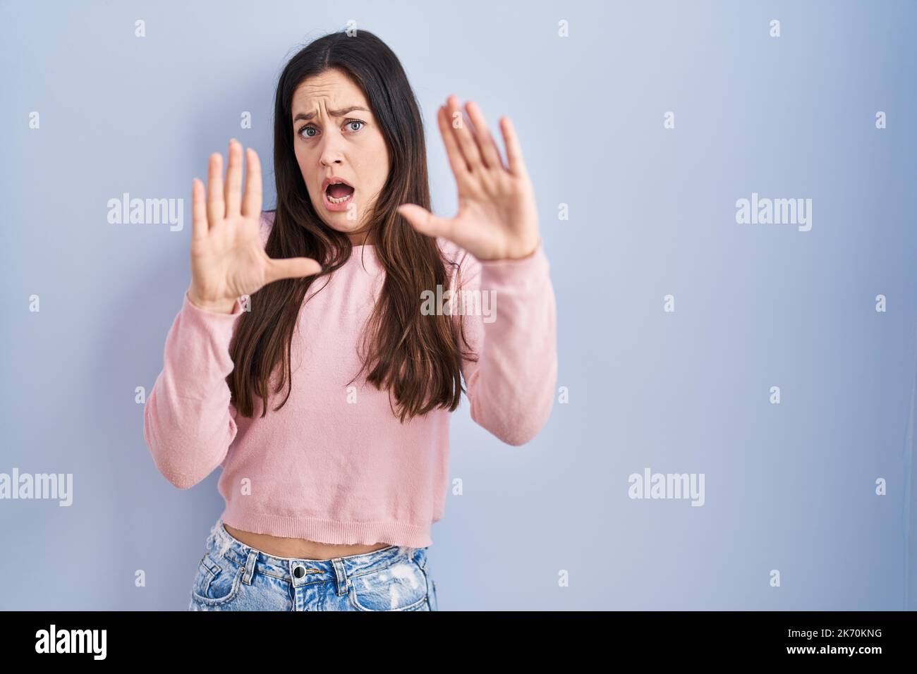 Young brunette woman standing over blue background afraid and terrified ...