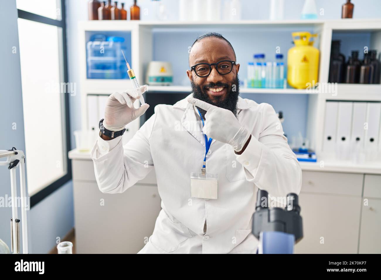 African american man working at scientist laboratory holding syringe smiling happy pointing with ...