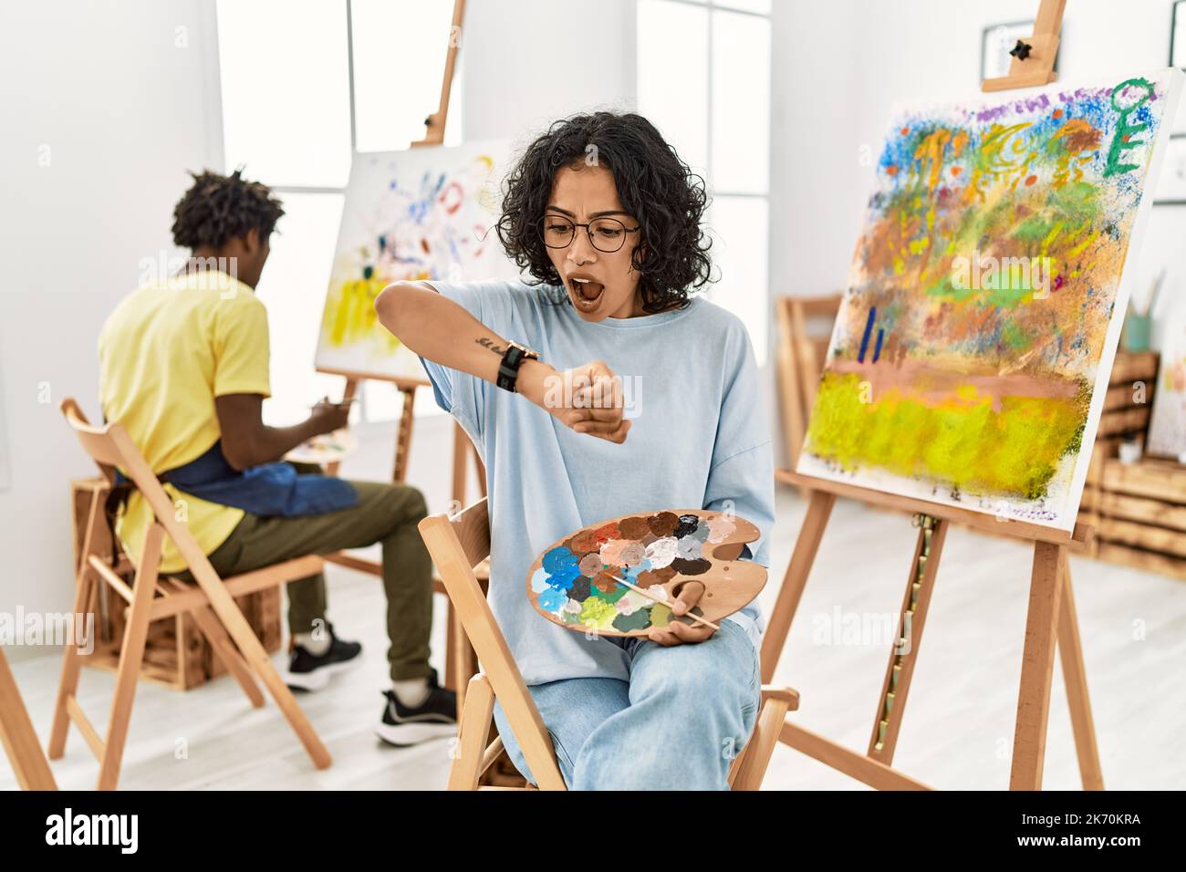 Young hispanic woman at art studio looking at the watch time worried ...