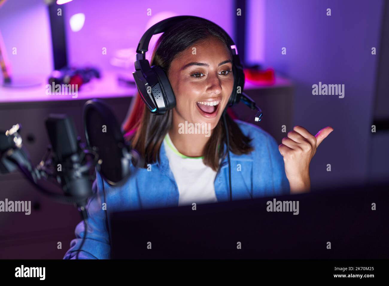 Young hispanic woman wearing headphones playing video games pointing ...