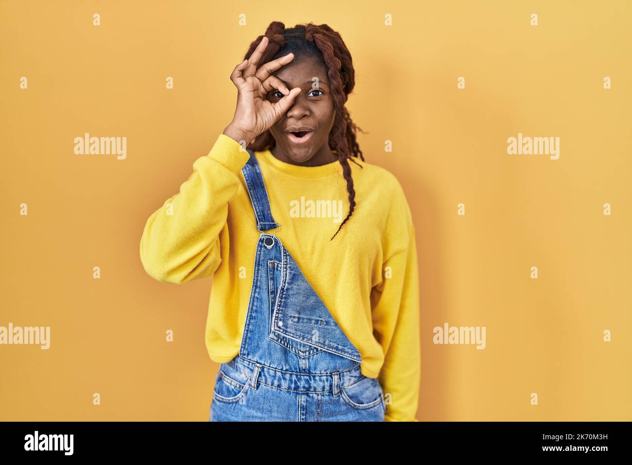 African woman standing over yellow background doing ok gesture shocked ...