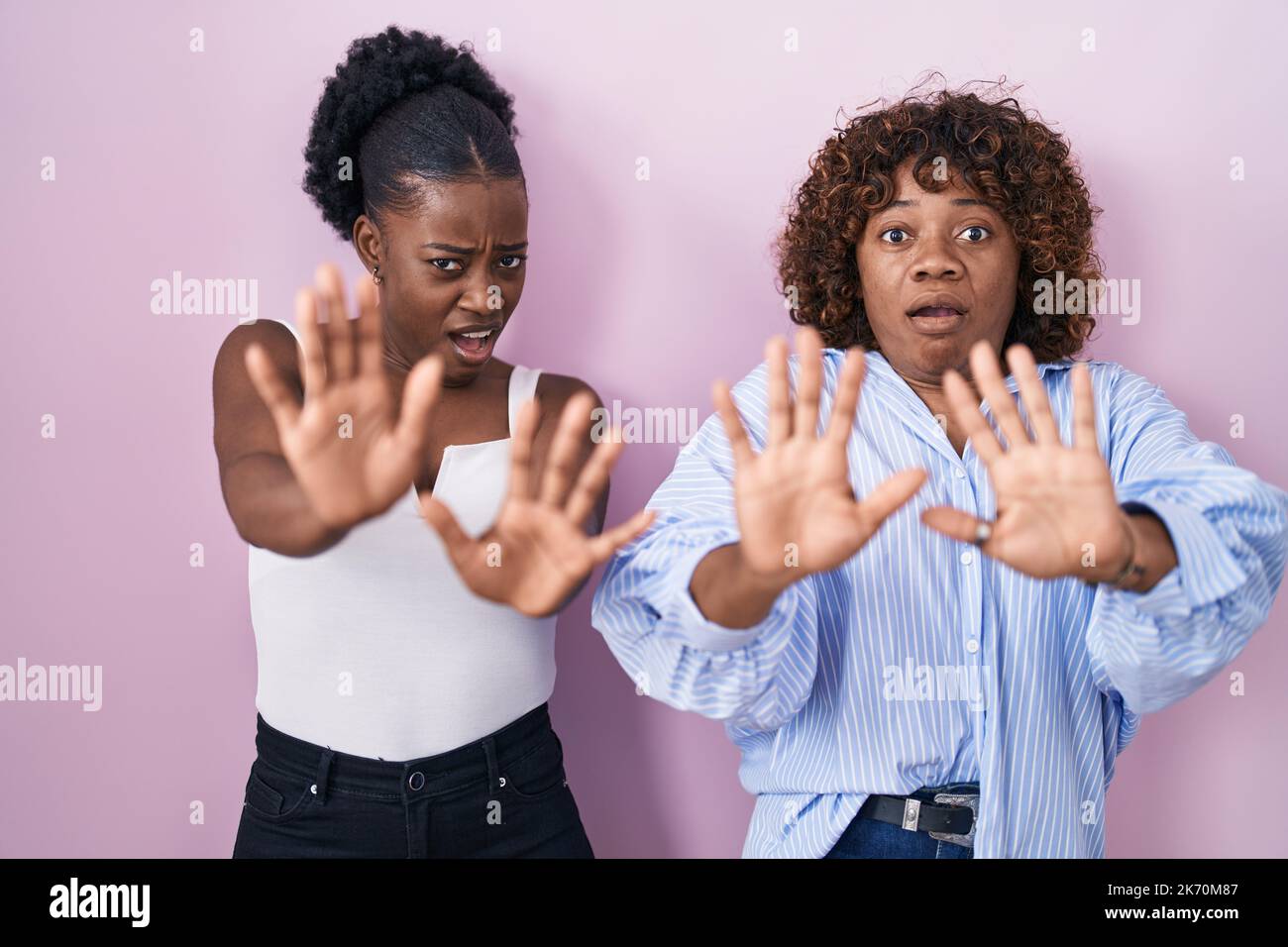 Two african women standing over pink background afraid and terrified ...