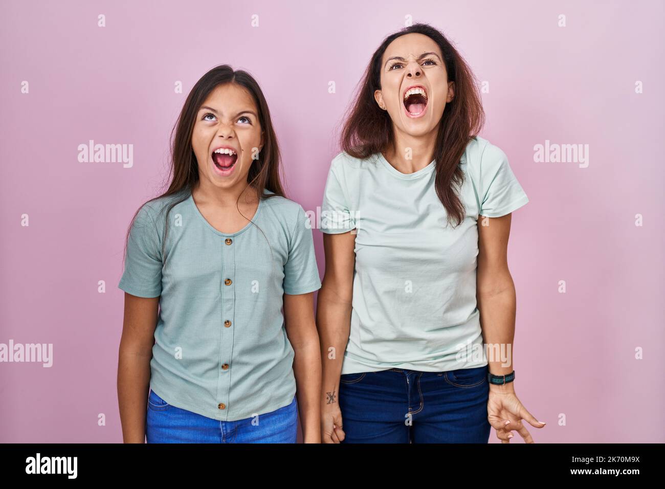 Young mother and daughter standing over pink background angry and mad ...