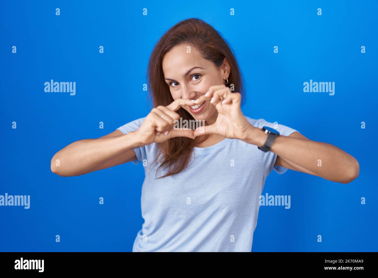 Brunette woman standing over blue background smiling in love doing ...