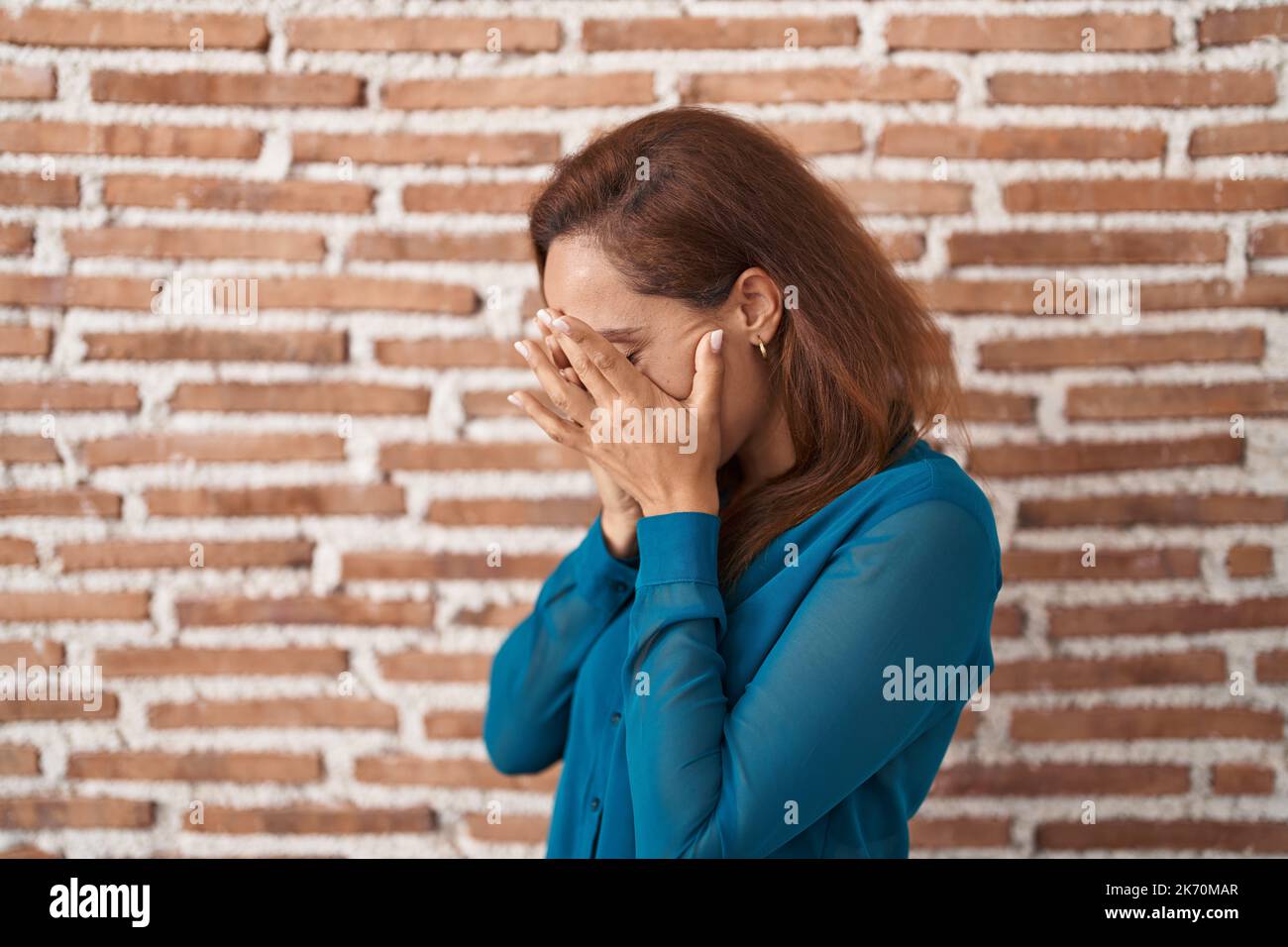 Brunette woman standing over bricks wall with sad expression covering ...