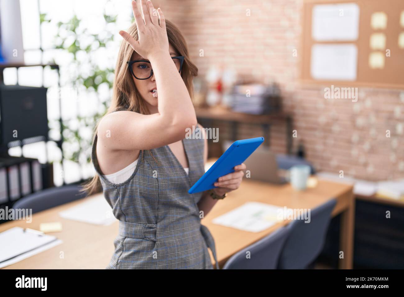 Caucasian woman working at the office wearing glasses surprised with ...