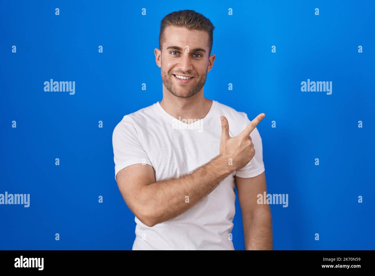 Young caucasian man standing over blue background cheerful with a smile ...