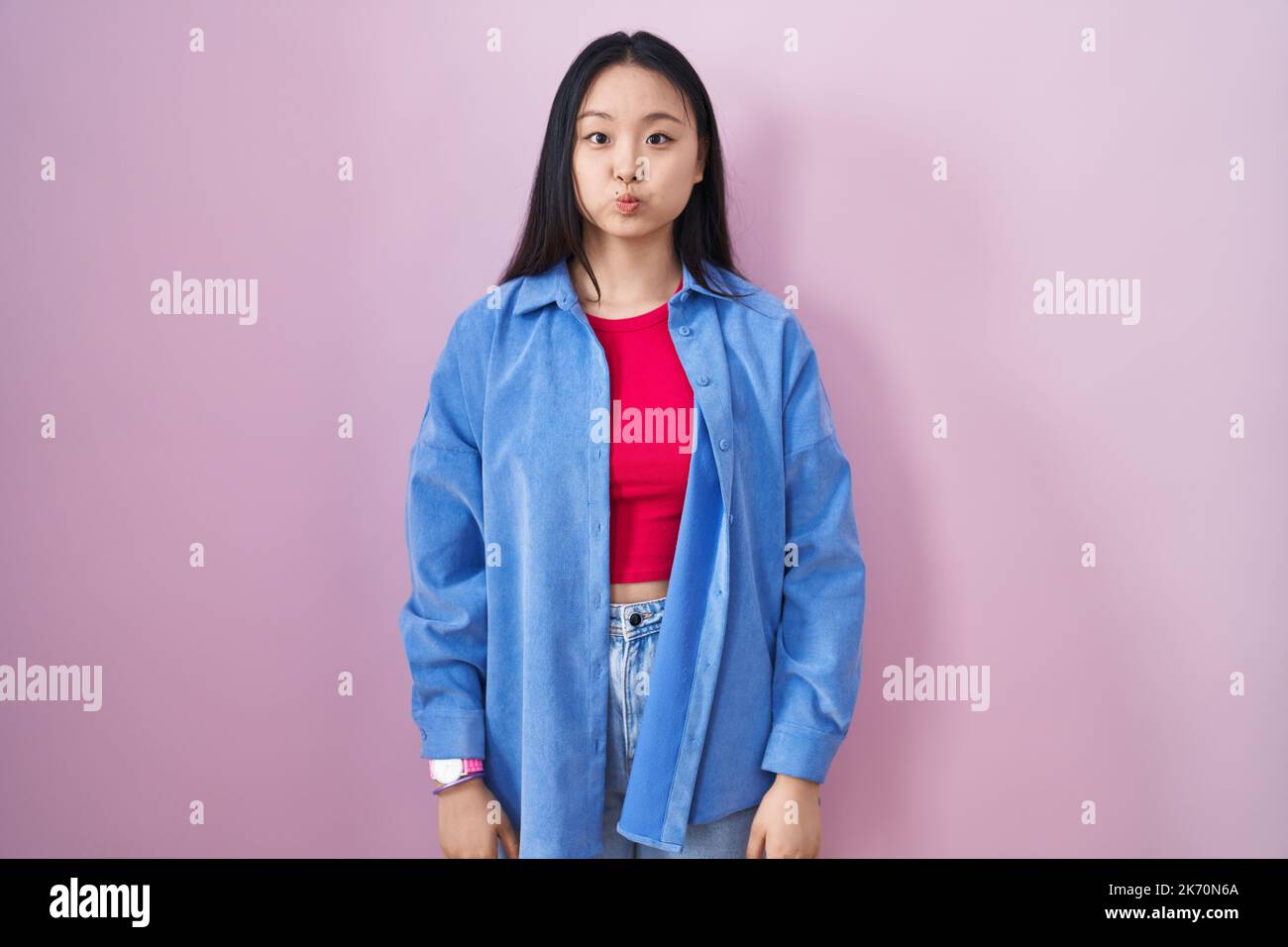 Young asian woman standing over pink background puffing cheeks with ...
