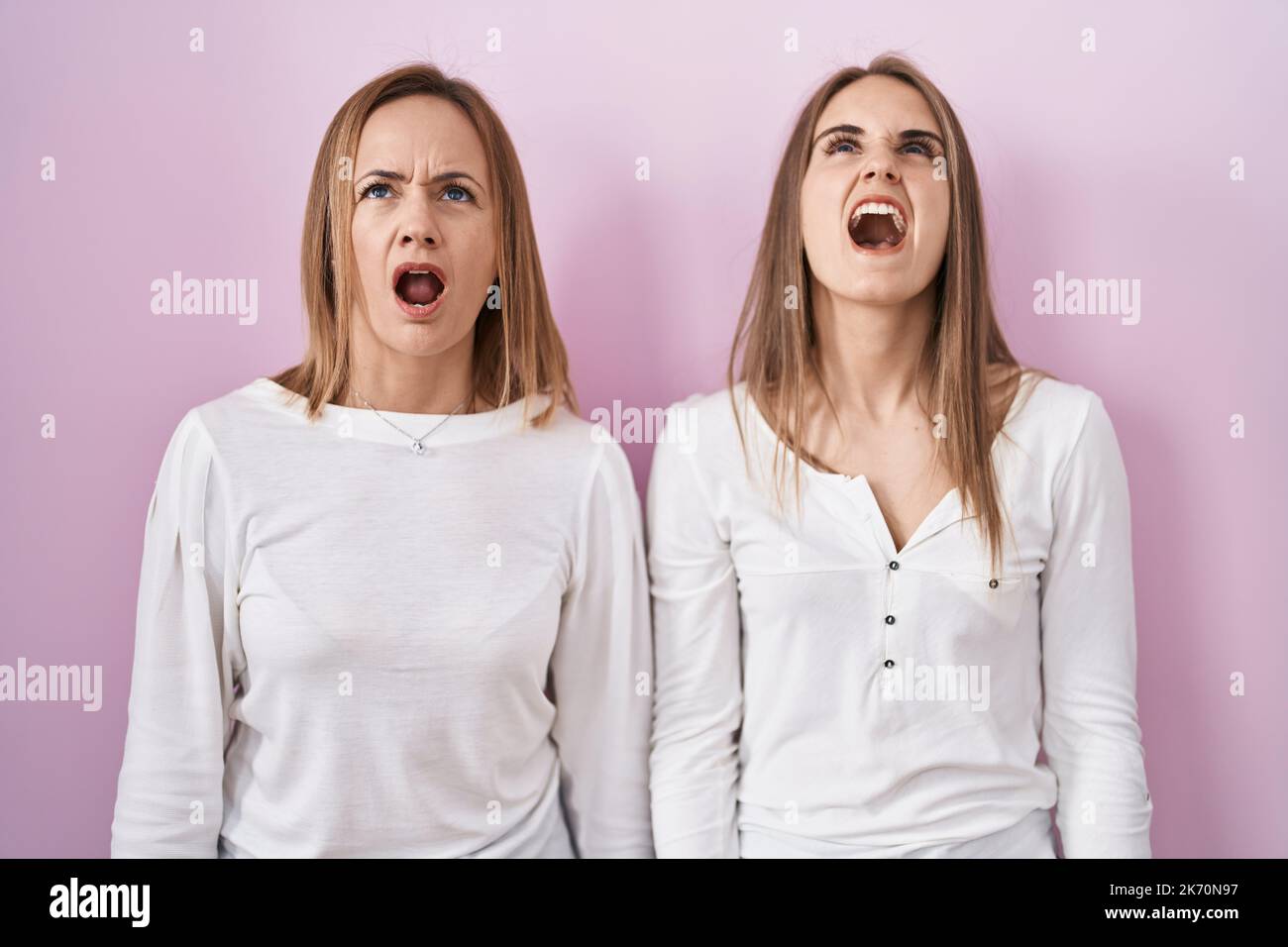 Middle age mother and young daughter standing over pink background ...