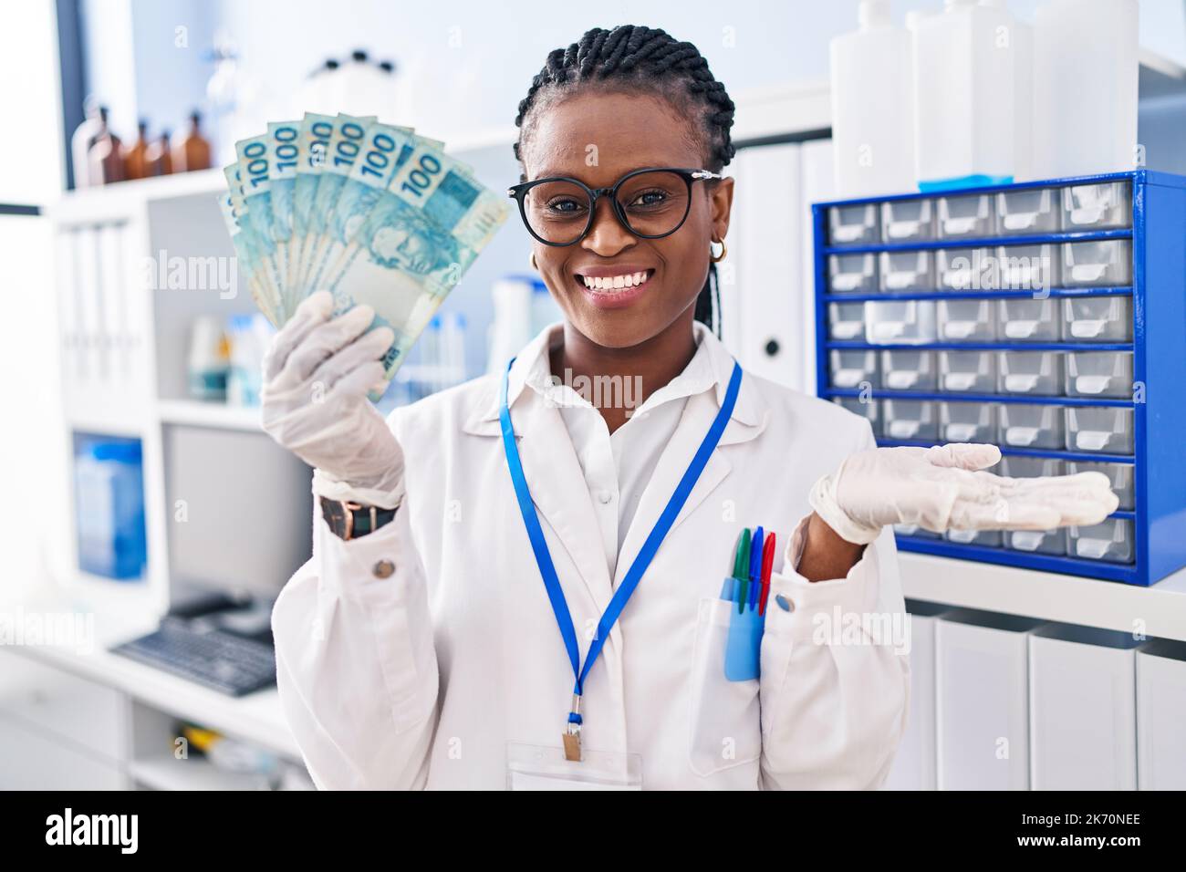 African woman with braids working at scientist laboratory holding money celebrating achievement ...